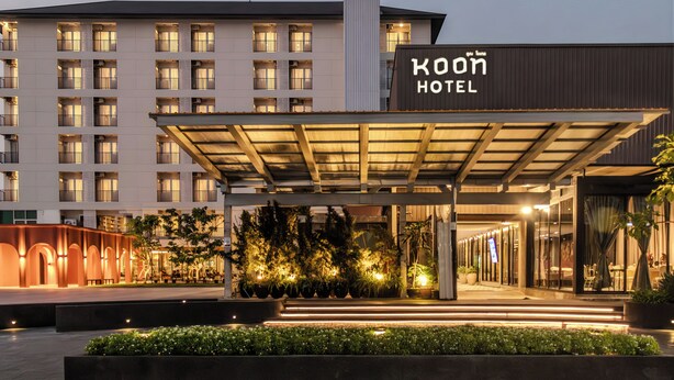 Um hotel com entrada coberta, várias varandas e uma placa com a inscrição 'Koon Hotel'.