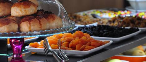 Buffet variado com diversos alimentos, incluindo doces e frutas, e um expositor de vidro.