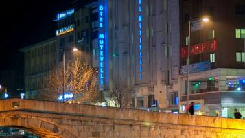 Um hotel com letreiros iluminados, uma ponte de pedra e um rio.