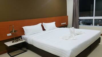 Cama bem arrumada com lençóis brancos e duas almofadas, luminária de cabeceira e janela com cortinas.