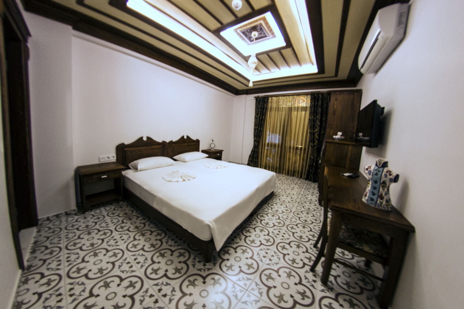 Quarto com cama, mesa de cabeceira, penteadeira, televisão e piso estampado.