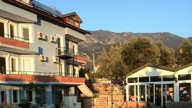 Área da piscina com espreguiçadeiras, um edifício com várias varandas e um cenário montanhoso.