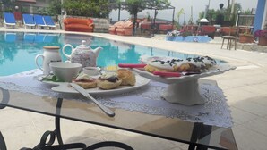 Mesa com chávena, biscoitos e bule junto a uma piscina.