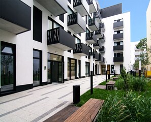 Um edifício moderno com varandas, grandes janelas e um pátio com bancos e vegetação.