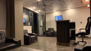 Um interior moderno com um balcão de recepção, área de estar e uma tela de televisão.