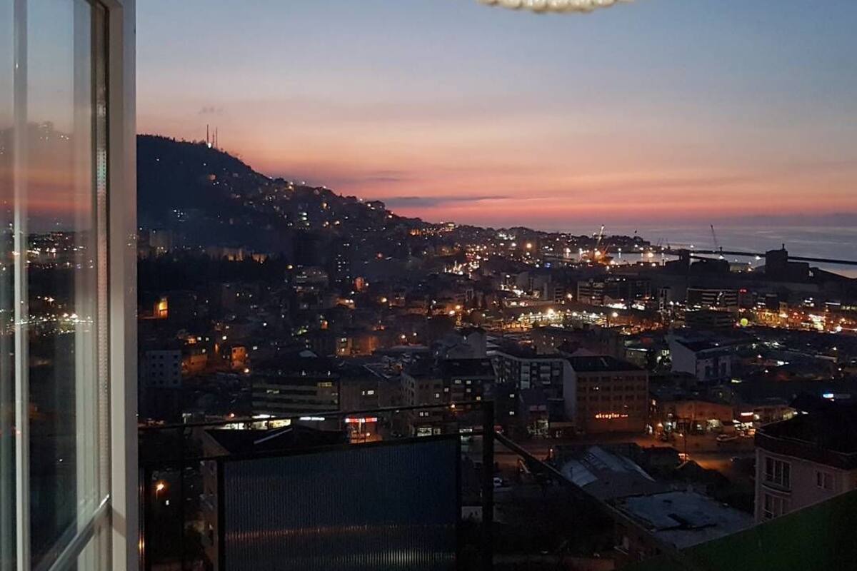 Vista urbana ao entardecer, com a costa, edifícios e uma colina ao longe.