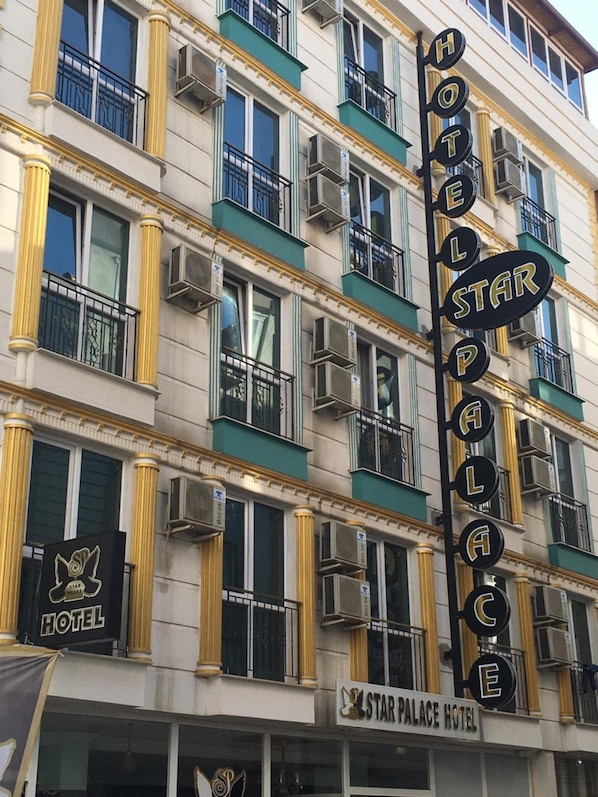 Um hotel com vários andares, varandas, aparelhos de ar condicionado e uma placa chamativa com a inscrição "Star Palace Hotel".