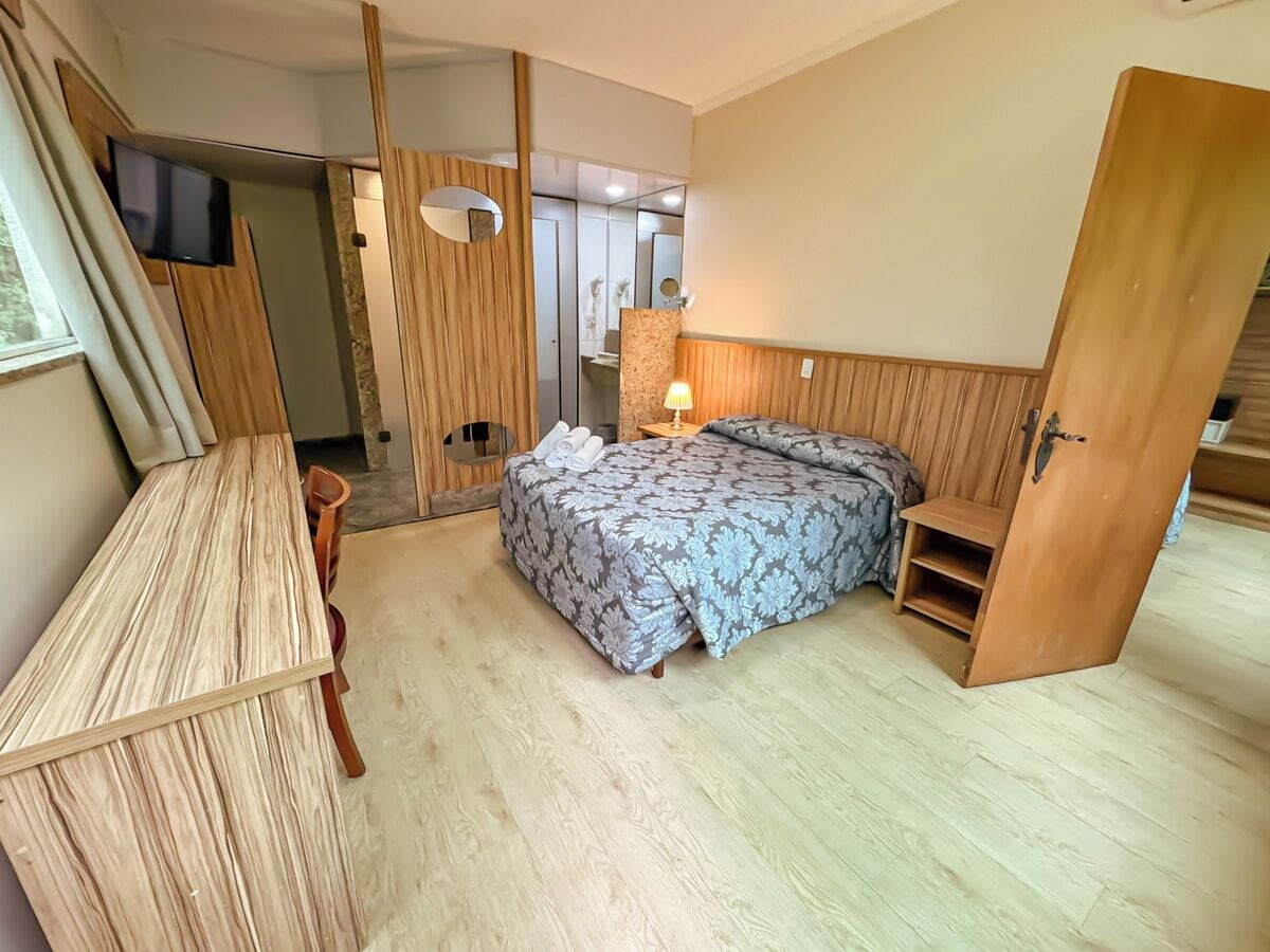 Um quarto com cama, escrivaninha, cadeira, televisão e guarda-roupa.