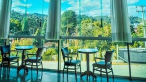 Quarto com grandes janelas que oferecem vista para uma paisagem montanhosa. Há várias mesas e cadeiras dispostas para refeições ou descanso.