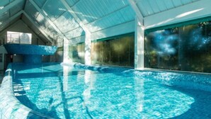 Piscina interna com água azul cristalina, teto inclinado e amplas janelas que permitem entrada de luz natural.