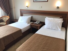 Quarto de hotel com duas camas, uma cadeira, mesa de cabeceira com telefone e arandelas na parede.