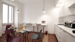 Uma cozinha moderna com armários brancos, uma área de jantar com mesa e cadeiras, e uma janela que ilumina naturalmente o espaço.