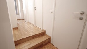 Um corredor com degraus de madeira que levam a uma porta branca com maçaneta e fechadura.