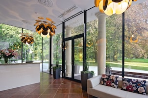 Uma área de recepção com um balcão branco, grandes janelas com vista para o verde e um sofá branco com almofadas florais.