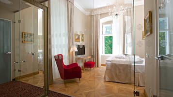 Quarto de hotel com um espelho grande, uma cadeira vermelha, uma cama e uma escrivaninha com abajur.