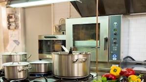 Uma cozinha industrial com eletrodomésticos de aço inoxidável, incluindo panelas em fogões, um forno grande e uma apresentação de legumes grelhados.