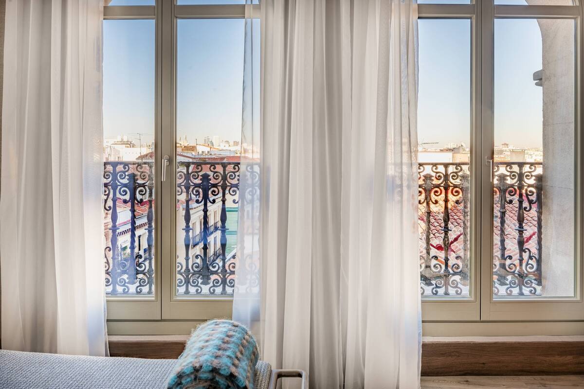 Quarto com uma grande janela, cortinas e vista para um horizonte urbano.