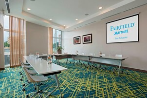 Uma sala de conferências com uma mesa comprida, cadeiras e uma tela de projetor exibindo "FAIRFIELD Marriott San Salvador".