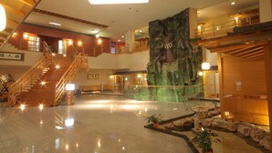 Um hall amplo com escadaria central, uma parede de escalada e uma pequena área de jardim.
