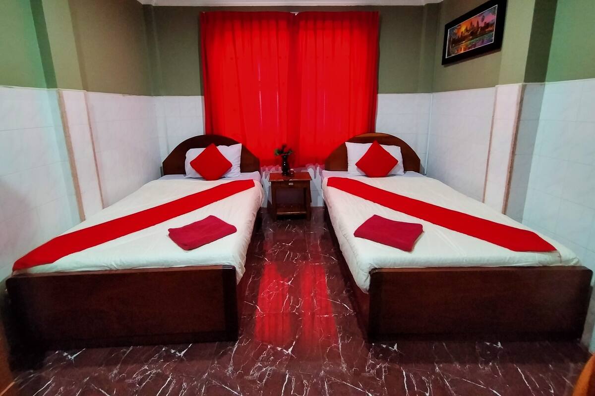 Quarto de hotel com duas camas, cortinas vermelhas, mesa de cabeceira e um quadro na parede.