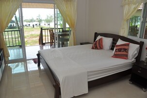 Quarto de hotel com uma cama grande, uma mesa de cabeceira e vista para um jardim através de uma porta de vidro deslizante.