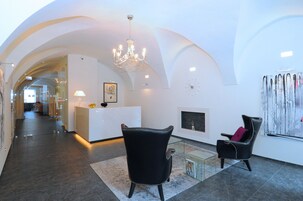Um interior moderno com um balcão de recepção, duas poltronas pretas, um candelabro e uma lareira.