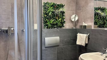 Uma casa de banho moderna com cabine de duche em vidro, sanita, lavatório e espelho fixado na parede.