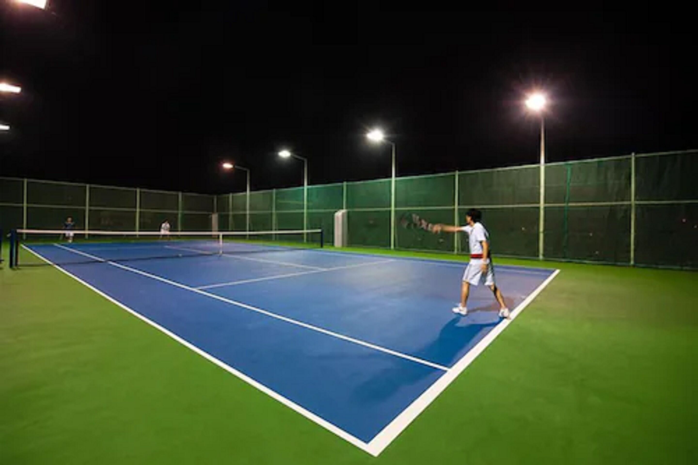 Uma quadra de tênis coberta com rede, iluminação e um jogador.