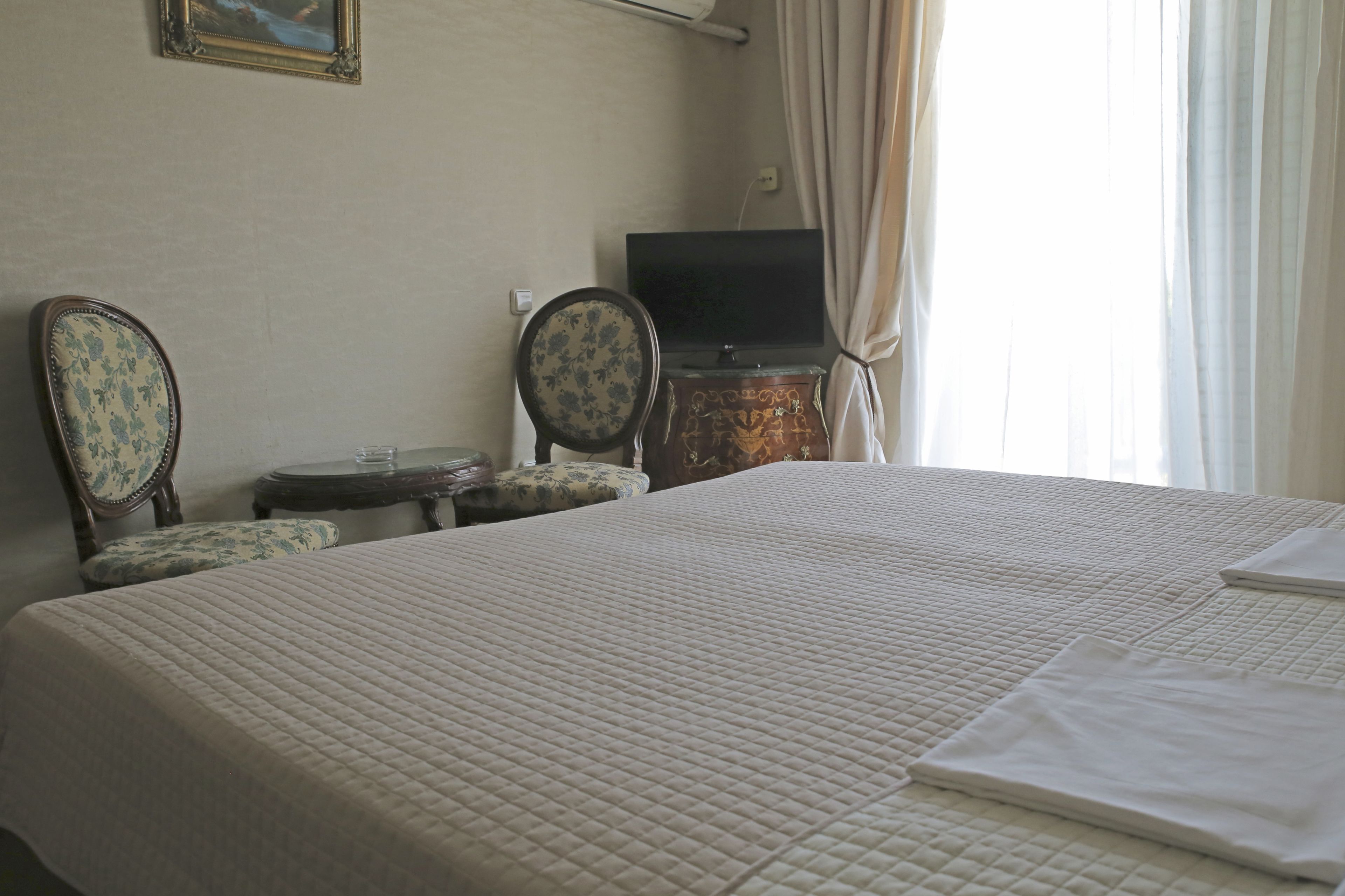 Quarto de hotel com uma cama grande, duas poltronas estofadas, uma mesa pequena, uma televisão e um armário.