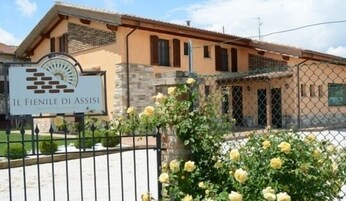 Um edifício com uma placa que diz "Il Fienile Di Assisi", cercado por uma grade de arame e rosas amarelas.