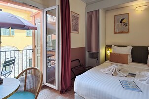 Quarto de hotel com cama, uma cadeira, uma mesa, varanda e porta.