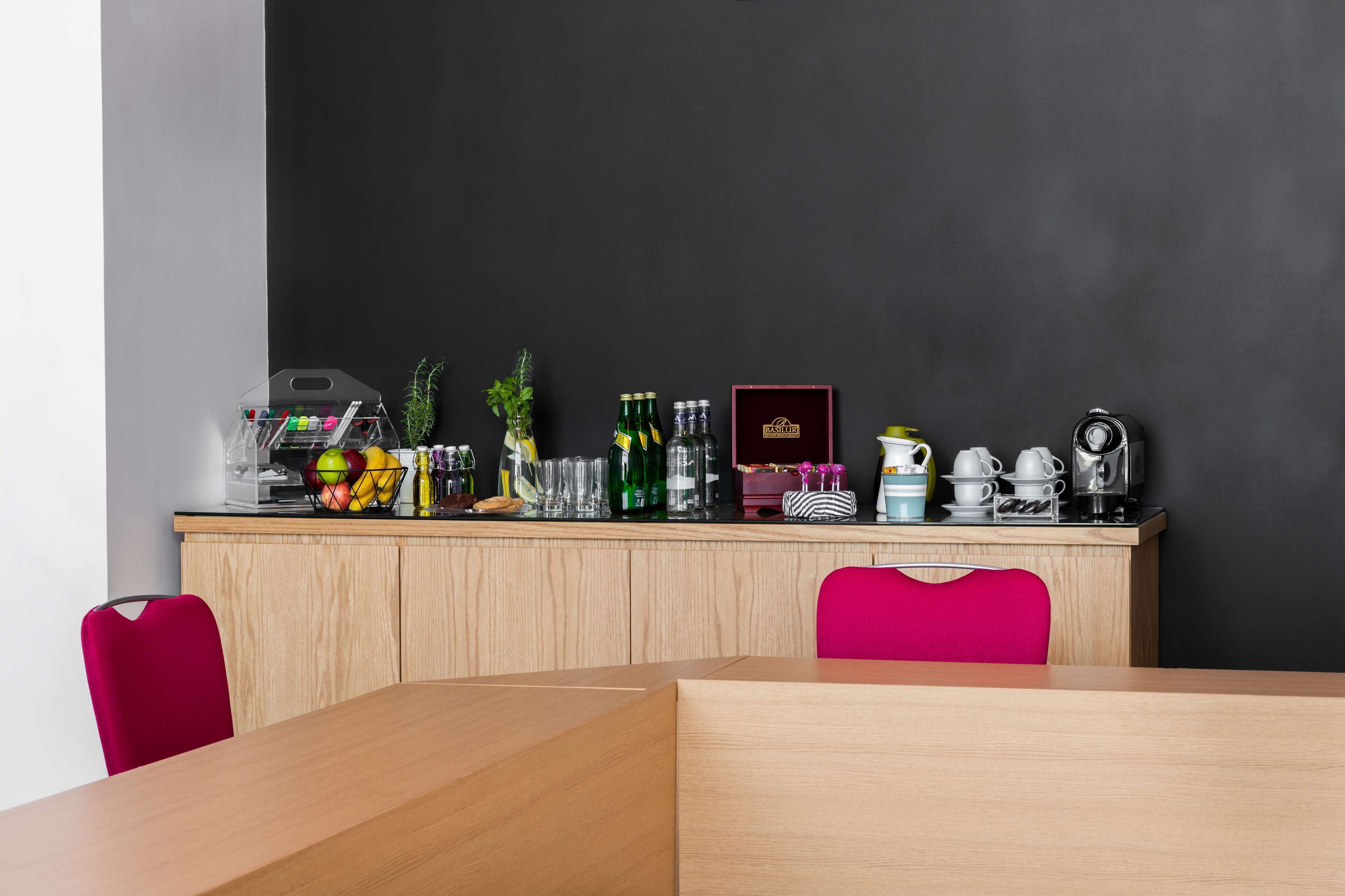 Uma sala de jantar moderna com uma mesa e cadeiras de madeira, uma parede preta e um balcão com diversos objetos, incluindo garrafas, uma caixa vermelha e utensílios de cozinha.