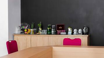 Uma sala de jantar moderna com uma mesa e cadeiras de madeira, uma parede preta e um balcão com diversos objetos, incluindo garrafas, uma caixa vermelha e utensílios de cozinha.