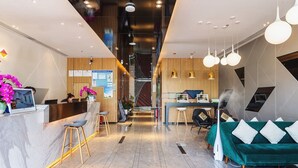 Um lobby de hotel moderno com uma mesa de recepção, área de estar e um sofá verde.
