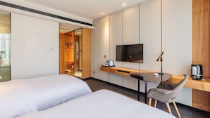 Quarto de hotel com duas camas, uma escrivaninha com televisão de tela plana, uma cadeira e uma máquina de café.