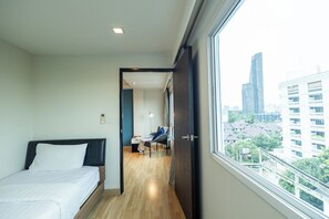 Quarto de hotel com cama, escrivaninha, cadeira e vista da cidade através de amplas janelas.