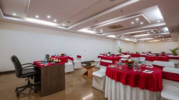 Sala de conferências com mesas redondas, cadeiras brancas e toalhas de mesa vermelhas. Há um púlpito de madeira e uma cadeira de escritório preta.