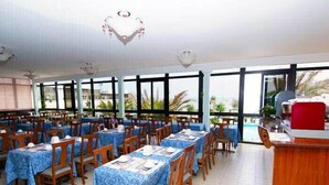 Uma ampla área de refeições interna com várias mesas e cadeiras, grandes janelas e vista para a piscina.