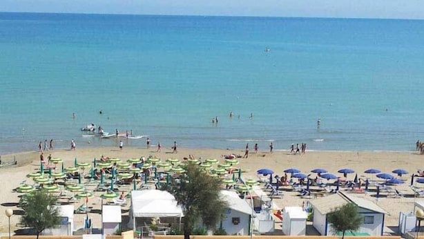 Uma praia com vários guarda-sóis e pequenas cabanas, sugerindo um ambiente de resort.