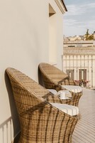 Duas poltronas de vime com almofadas, posicionadas em frente a uma parede numa área de pátio com piso de azulejos.