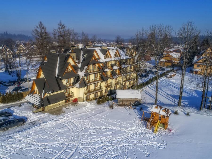 Um chalé grande, de vários andares, com telhado inclinado, rodeado por neve no chão e nas árvores.