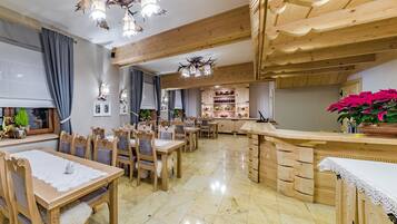 Uma ampla sala de jantar com mesas e cadeiras de madeira, uma área de cozinha com armários de madeira e um teto com design de madeira único.
