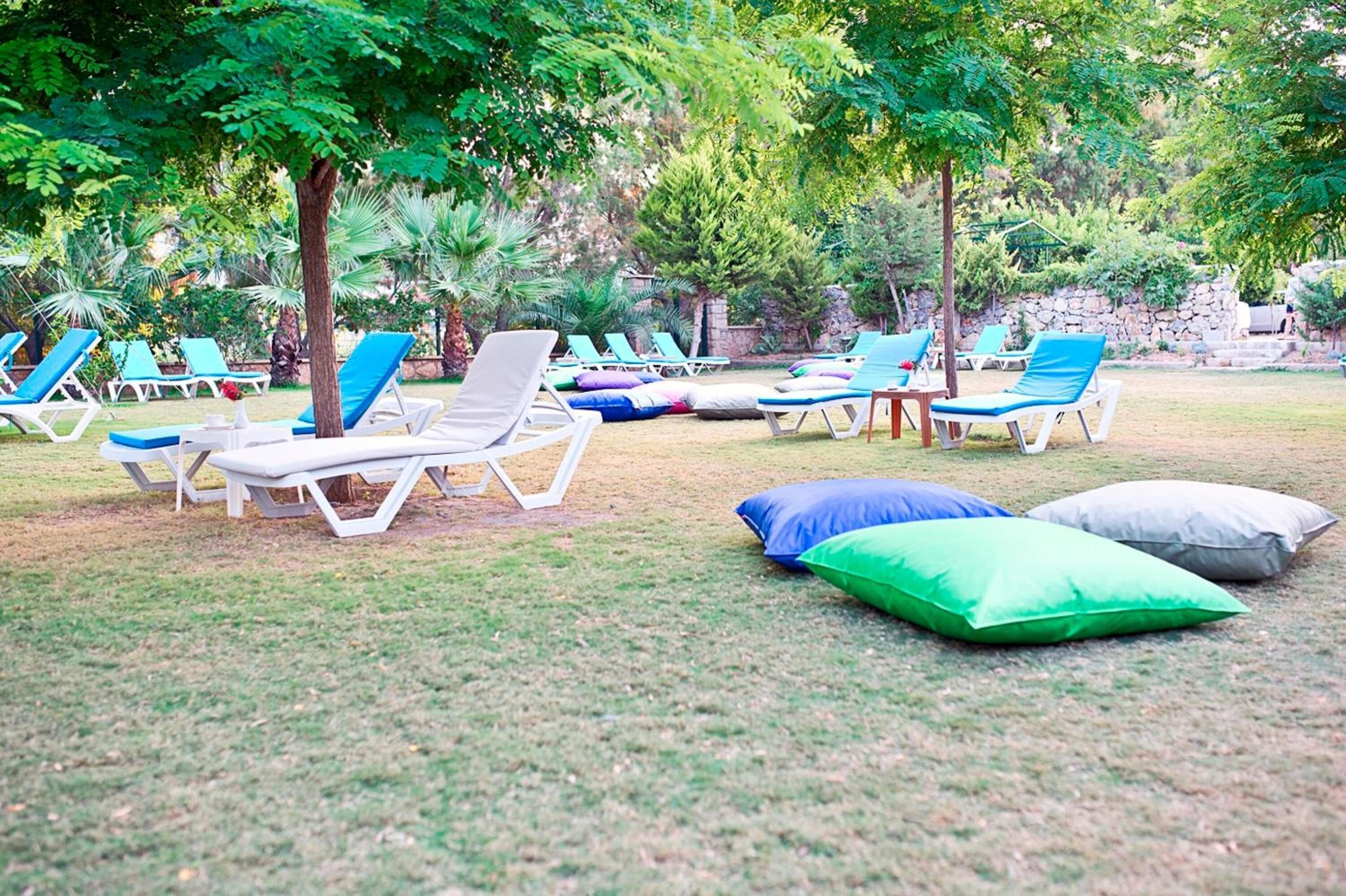 Uma área de jardim com várias cadeiras de descanso e mesas, cercada por árvores e vegetação.