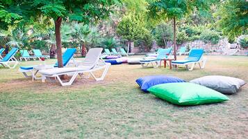 Uma área de jardim com várias cadeiras de descanso e mesas, cercada por árvores e vegetação.