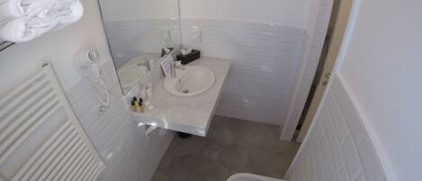 Um banheiro compacto com pia branca, espelho, vaso sanitário e porta-toalhas.