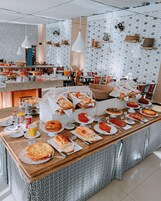 Disposição de buffet com diversos alimentos e área de refeições com cadeiras e mesas.