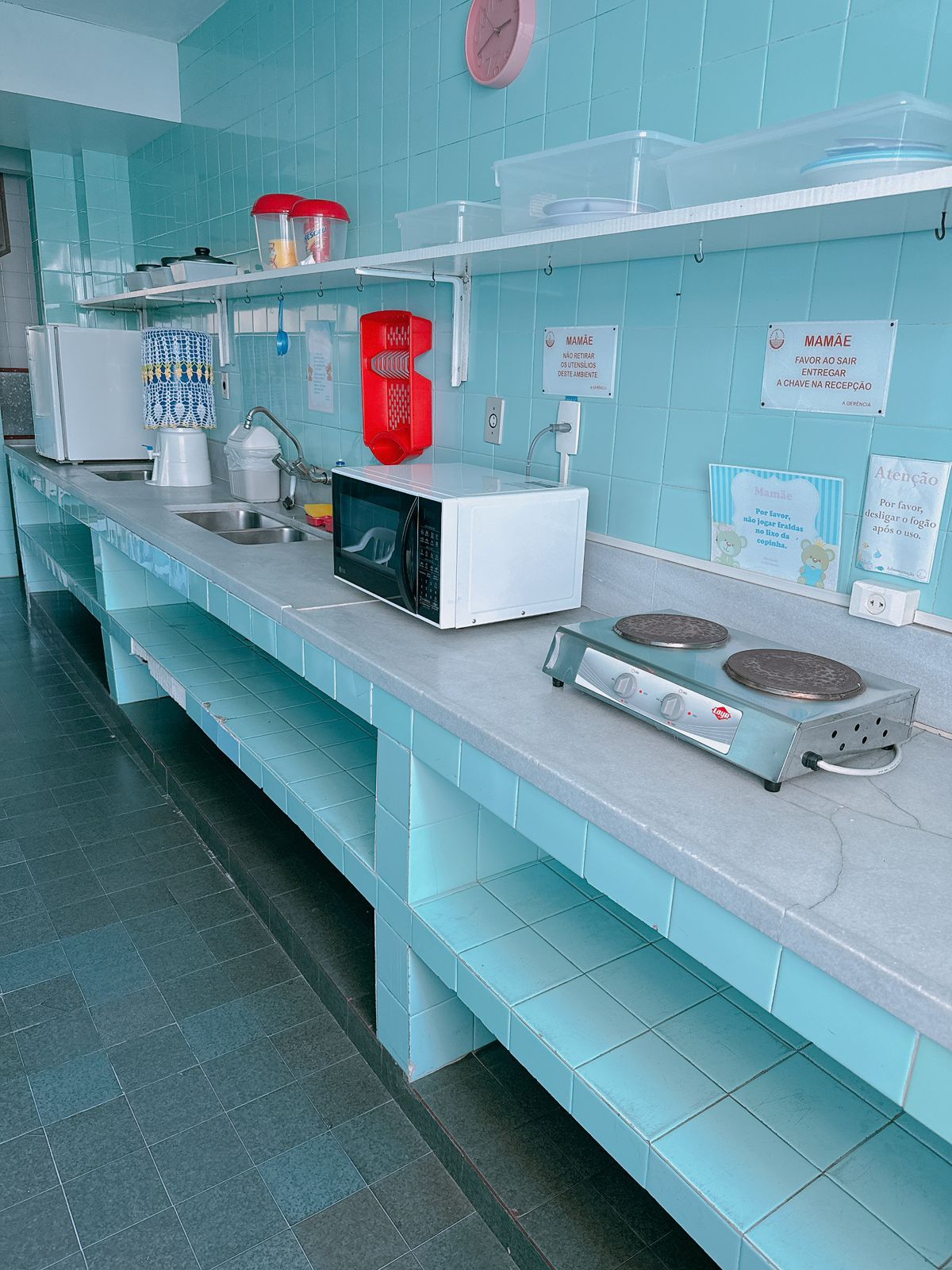 Cozinha equipada com micro-ondas, fogão e diversos utensílios de cozinha. Há placas na parede e um relógio sobre a pia.