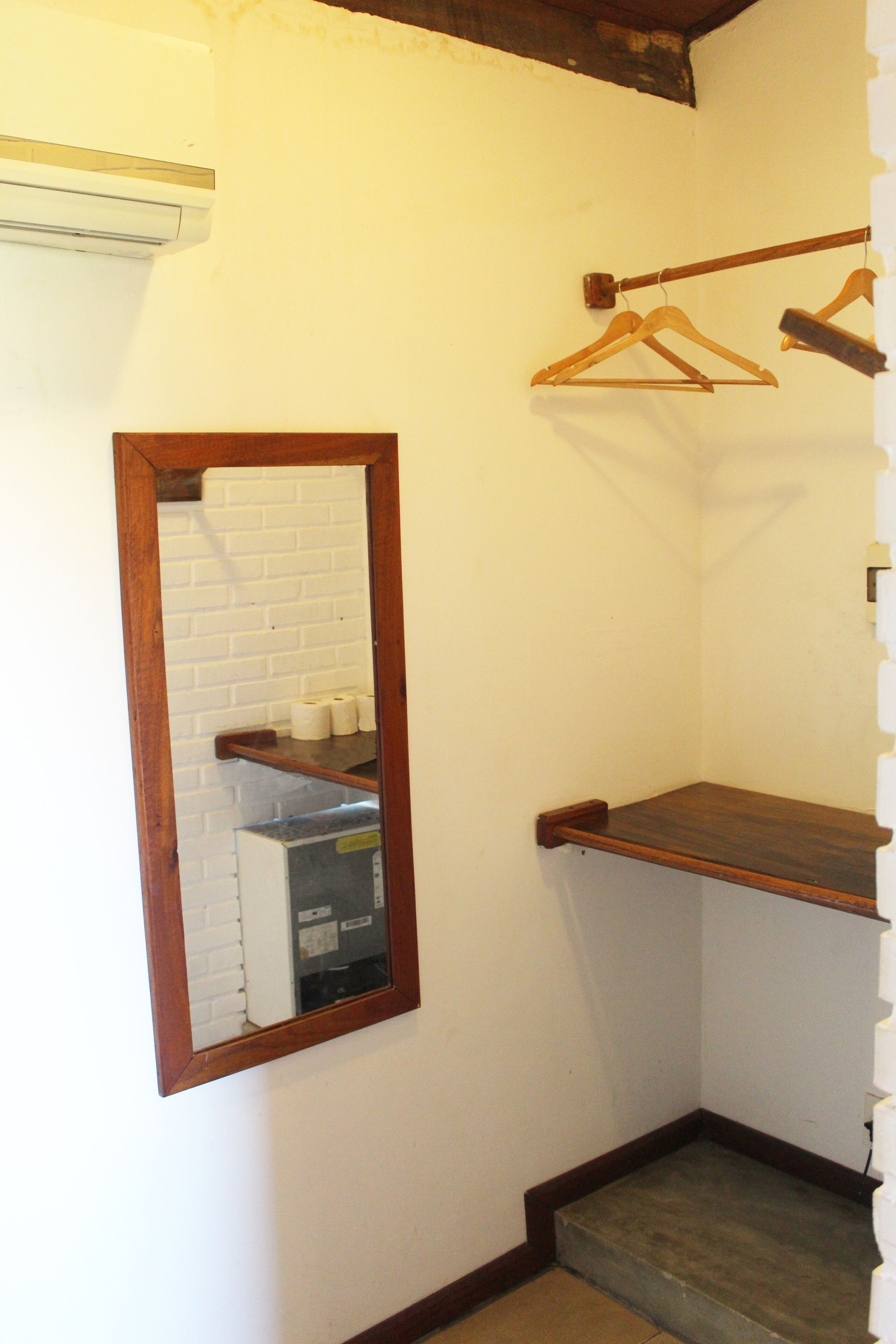 Casa de banho nos cantos com uma prateleira de madeira, um espelho com padrão de tijolo e um porta-casacos de madeira.