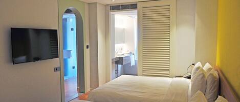 Quarto de hotel com duas camas, televisão presa à parede e banheiro visível por uma porta aberta.