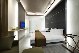 Quarto de hotel moderno com uma cama grande, televisão, secretária e um espaço de estar.